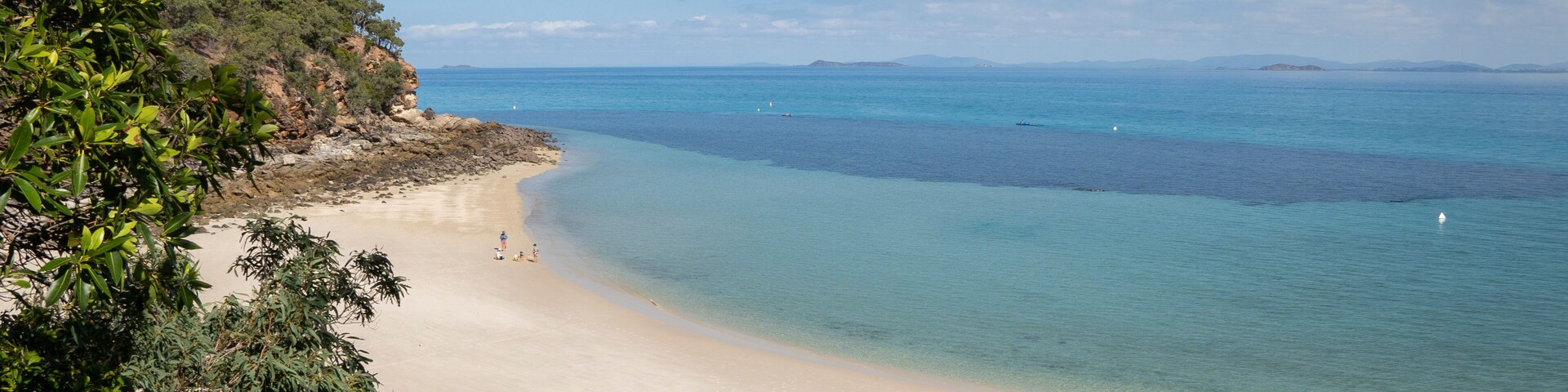 Uma praia com águas turquesa cristalinas, areal arenoso e vegetação verdejante.
