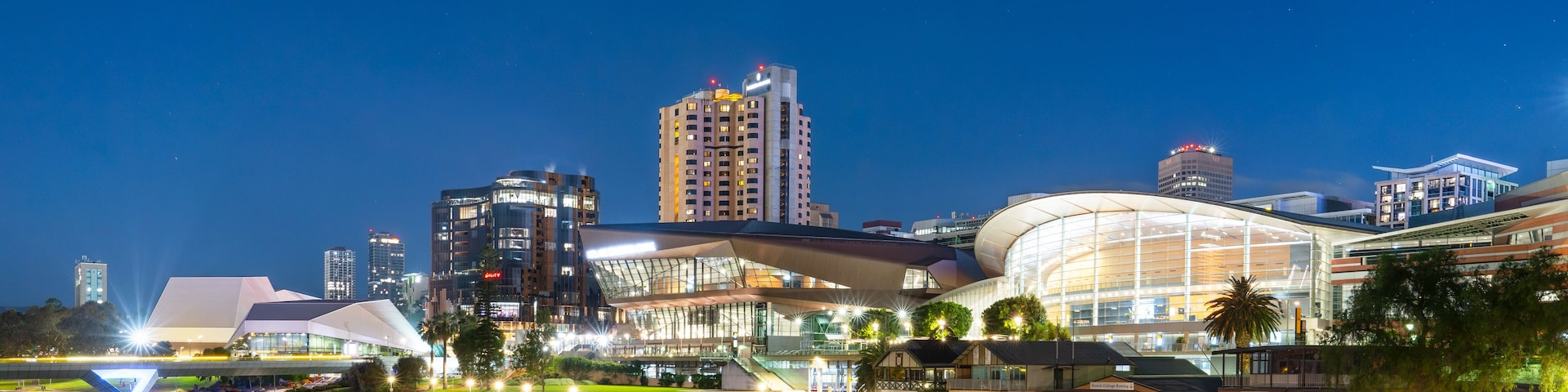 Paisagem urbana noturna com edifícios iluminados, um corpo d'água refletor e uma estrutura arquitetônica moderna.