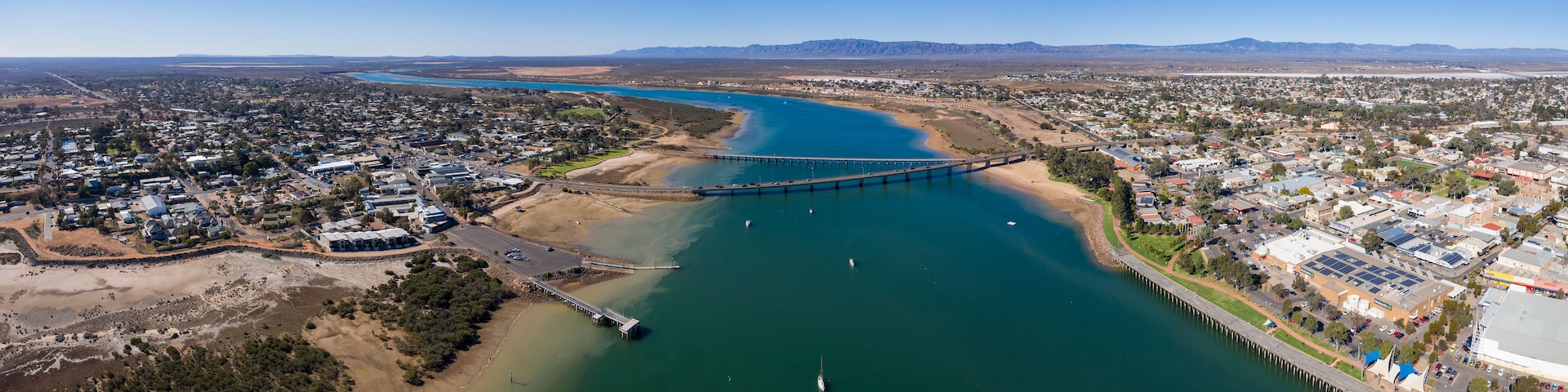 Uma cidade costeira com uma ponte sobre um rio, rodeada por montanhas.