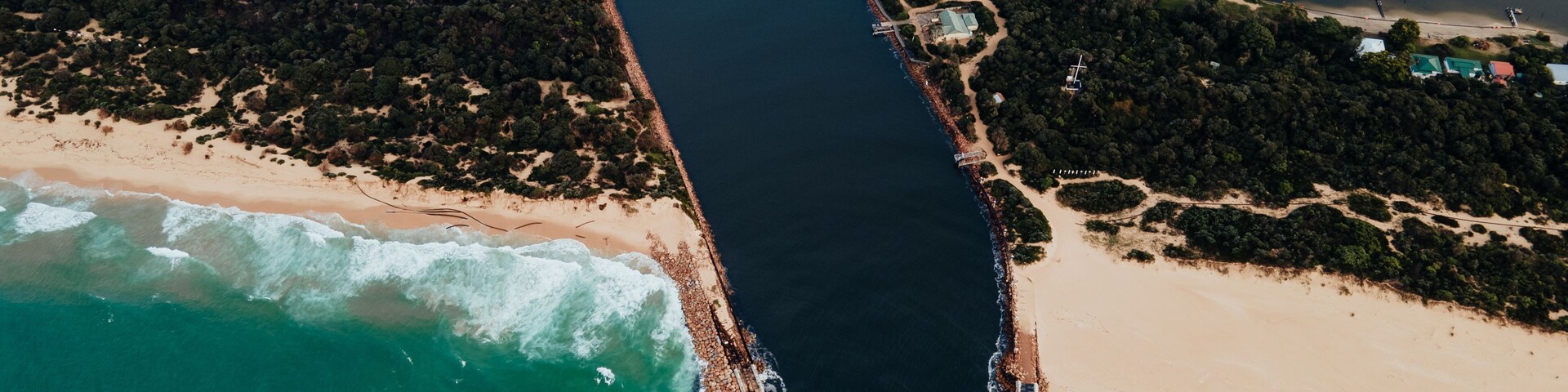 Vista aérea de uma área costeira com praia de areia, um canal estreito e uma ilha com vegetação densa.