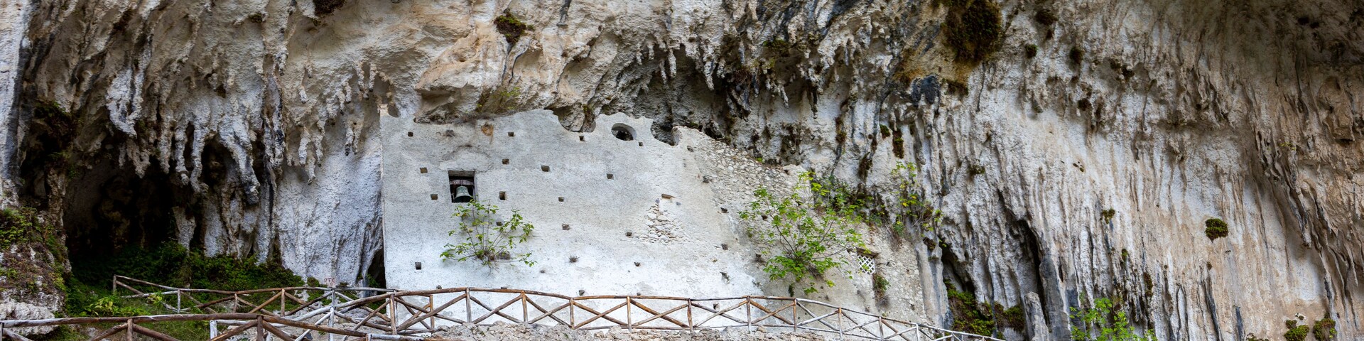 Entrada de uma caverna com cerca de madeira e uma pequena janela.