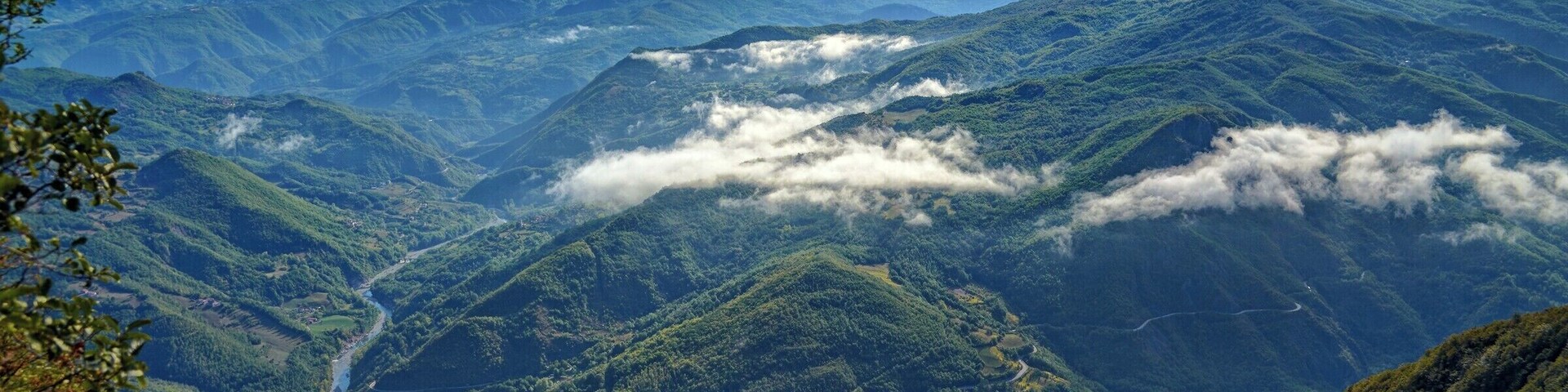 Paisagem montanhosa com vales verdejantes e um rio serpenteando pelo terreno.