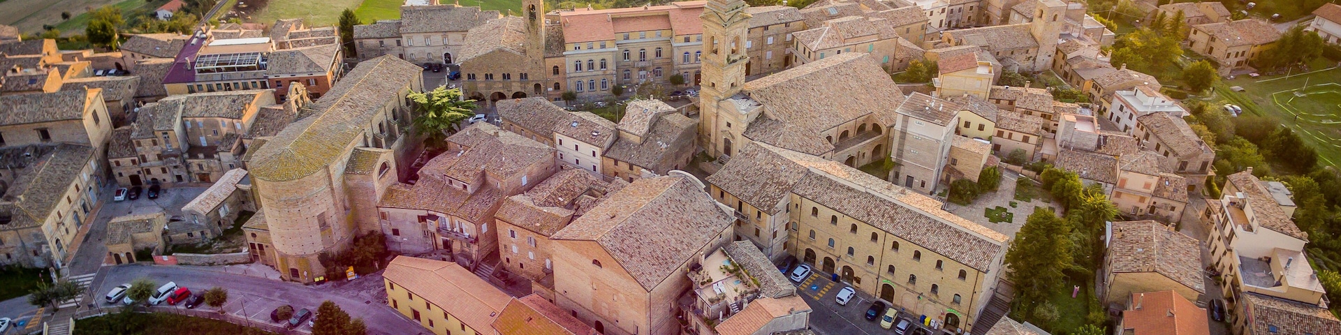 Vista aérea de uma cidade histórica, com uma torre de igreja imponente, ruas estreitas e campos agrícolas ao redor.