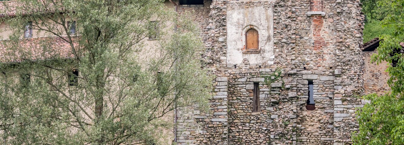 Uma torre de pedra com telhado em tijolos, rodeada por vegetação exuberante e árvores.