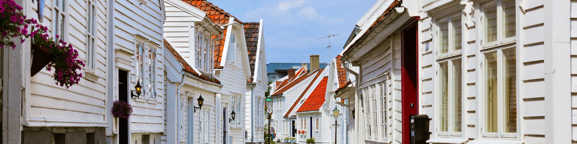 Rua de paralelepípedos flanqueada por edifícios brancos com telhados vermelhos e caixas de flores.
