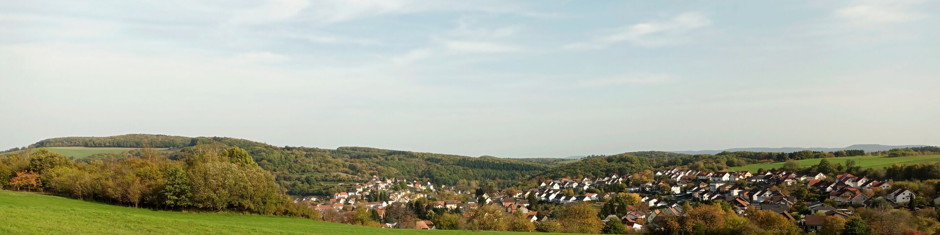 Paisagem rural com colinas ondulantes, uma aldeia e um campo verde.