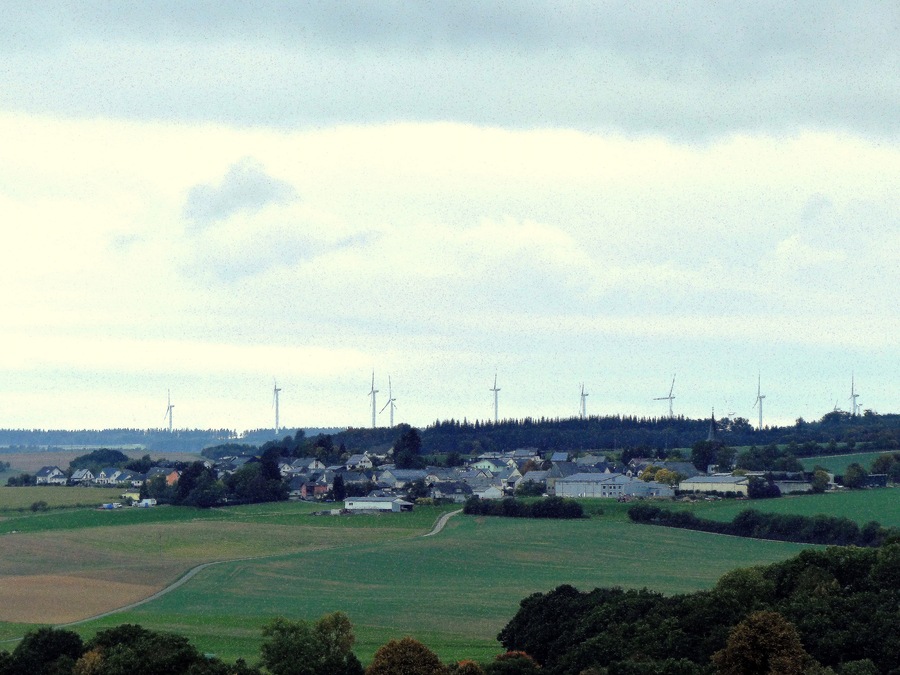 Paisagem rural com turbinas eólicas, casas e campos.