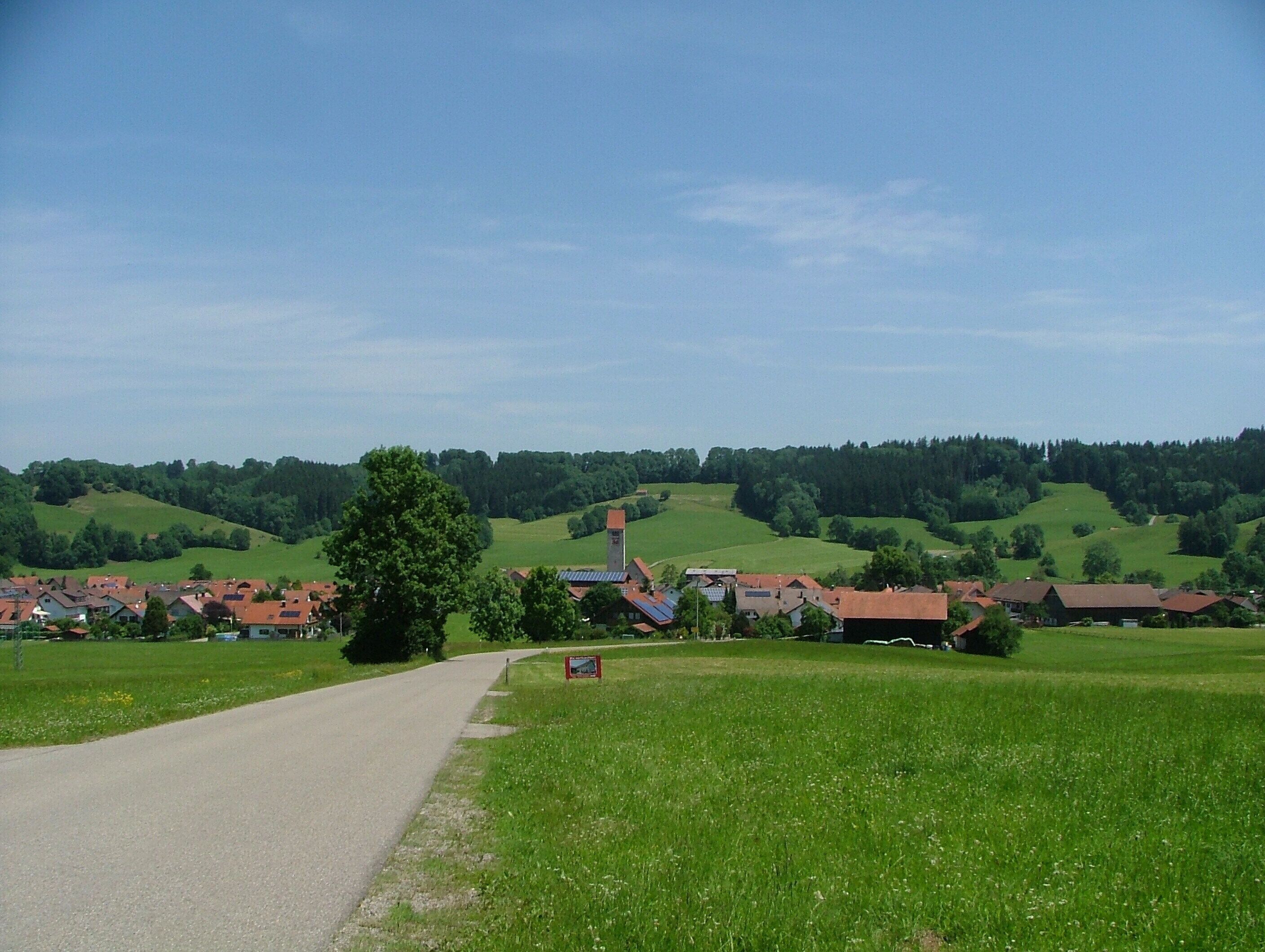 Paisagem rural com estrada, casas e colinas ondulantes.