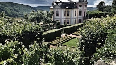 Um edifício histórico com jardim e montanhas ao fundo.