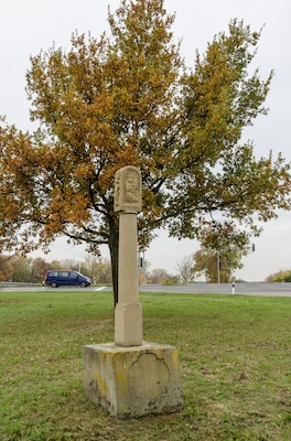 Um monumento de pedra com cabeça esculpida em um campo gramado, com uma árvore ao fundo.