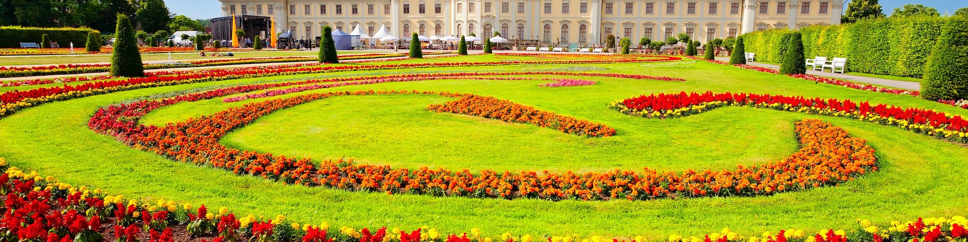 Um palácio imponente com um jardim simétrico, destacando canteiros de flores vibrantes e gramados bem cuidados.