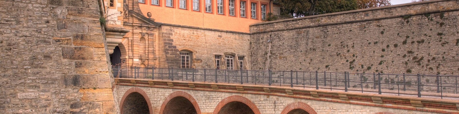 Um edifício histórico de pedra com telhado vermelho, parede de pedra e uma série de arcos.