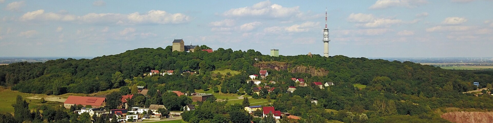 Paisagem acidentada com uma torre imponente, vegetação exuberante e edifícios dispersos.