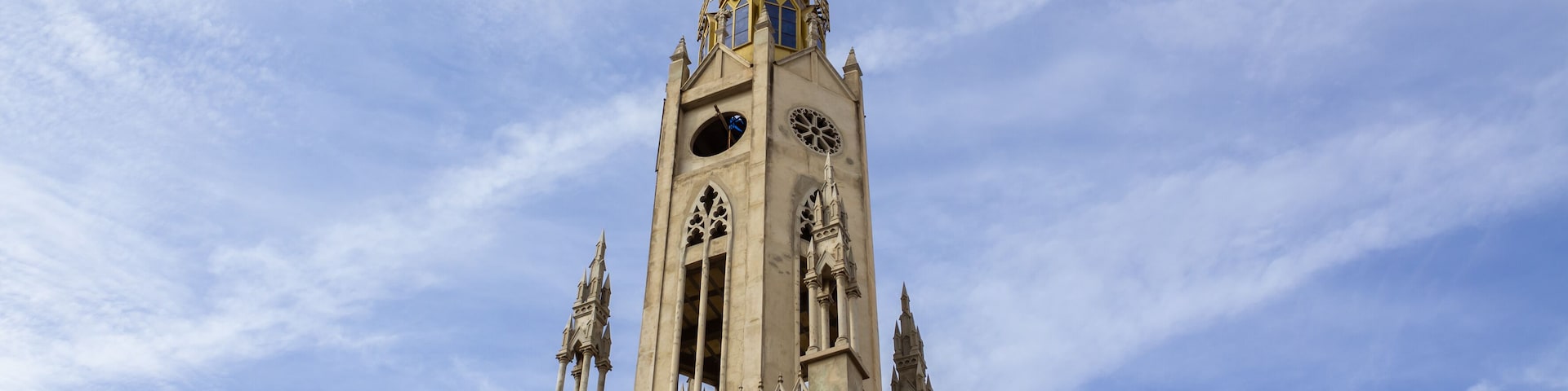Uma torre alta de igreja com uma cruz no topo, desenhos complexos nas janelas e um relógio.