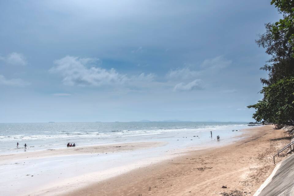 Uma praia com pessoas caminhando e sentadas, uma orla arenosa e o oceano.
