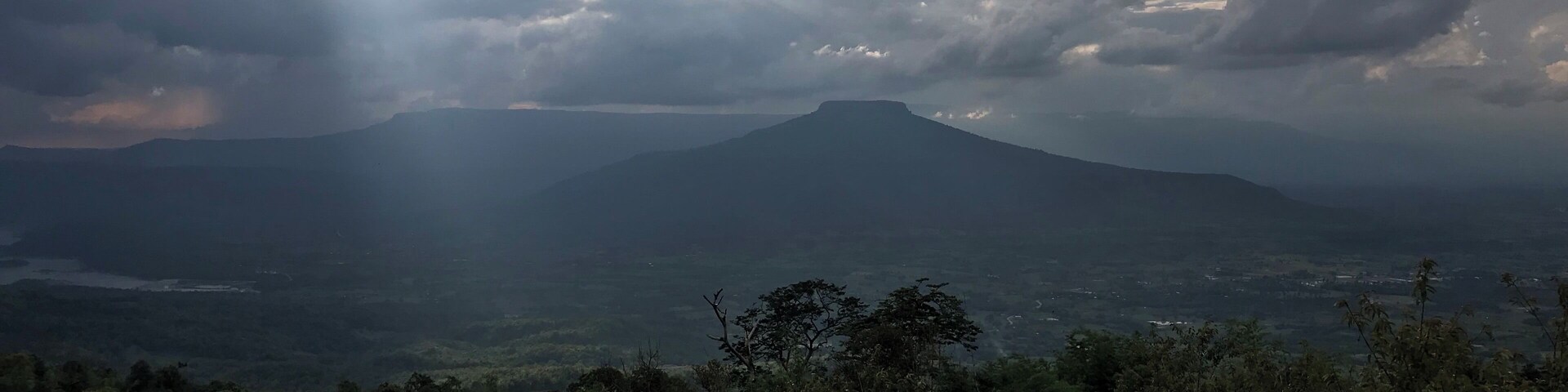 Paisagem montanhosa com um pico imponente, rodeado por uma floresta densa e um vale abaixo.