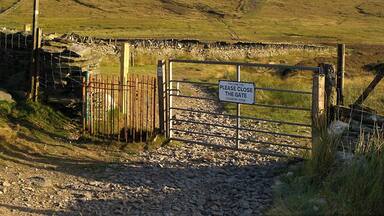 Paisagem rural com um portão e uma placa que diz 'PLEASE CLOSE THE GATE'.