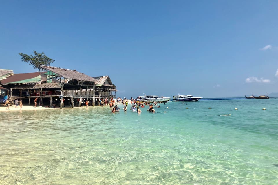 Uma praia com águas turquesa cristalinas, estruturas de madeira e barcos.