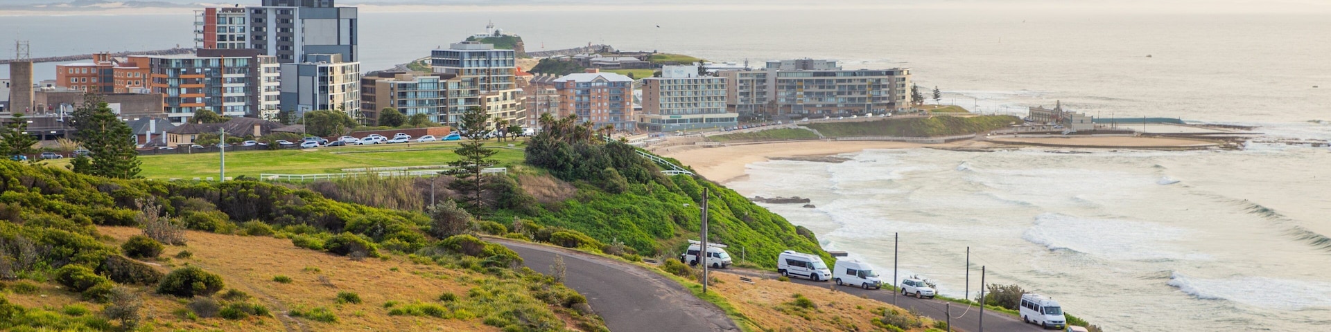 Uma estrada costeira com veículos, uma praia e edifícios residenciais.