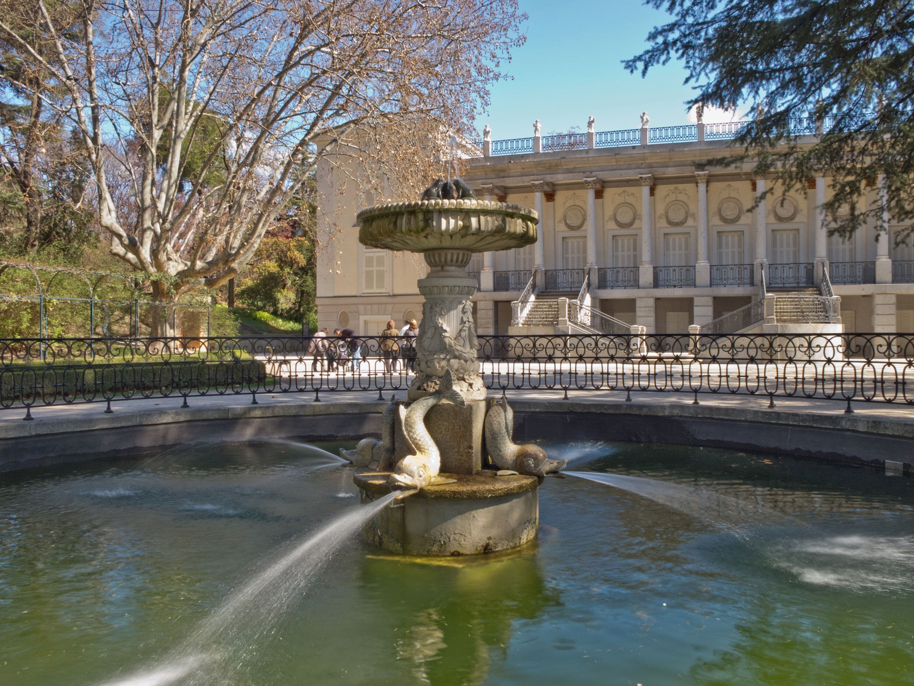 Uma fonte com estátua de peixe em um parque, com um edifício ao fundo.