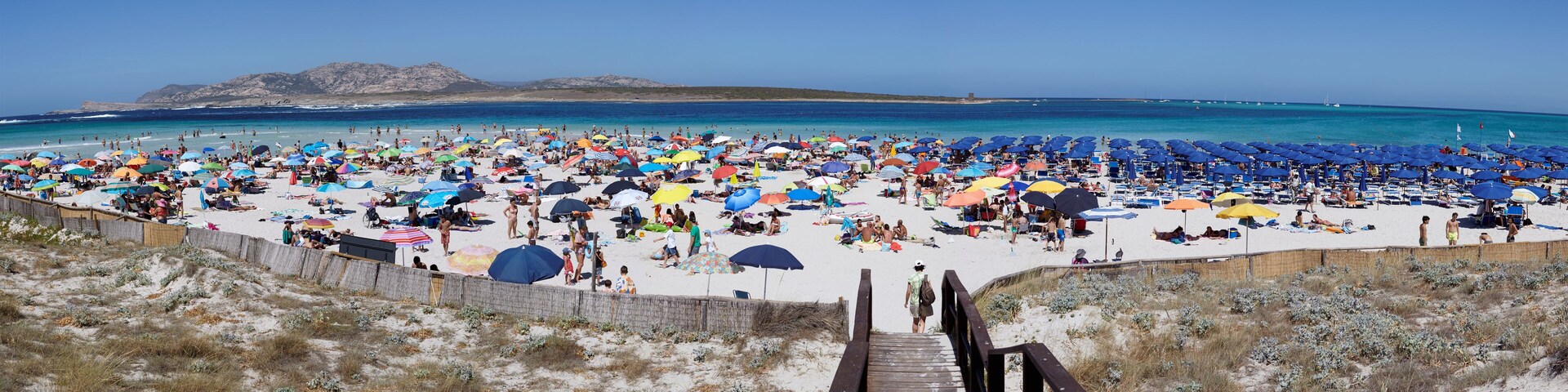 Praia cheia, com muitos guarda-sóis e pessoas.