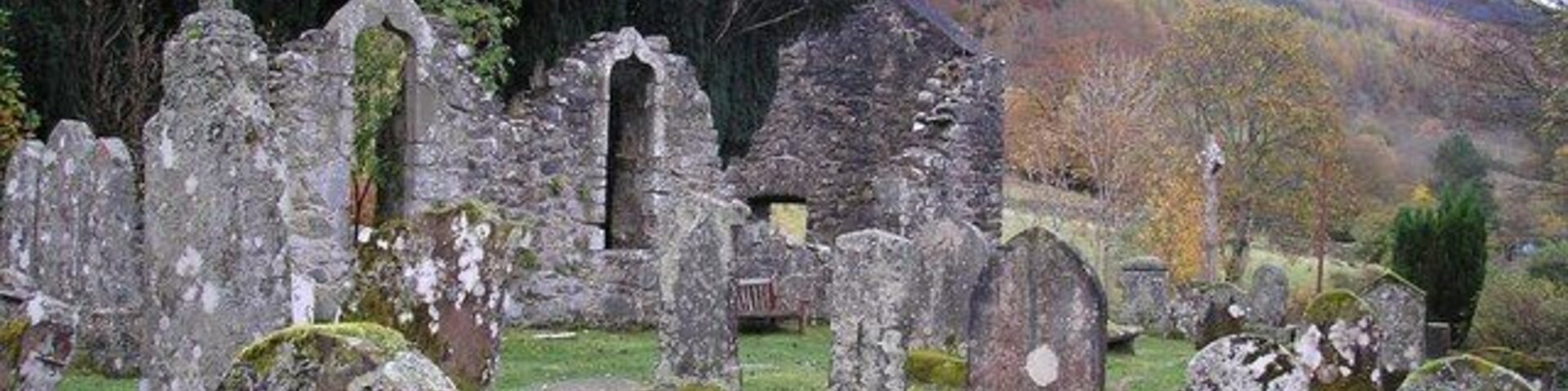 Um cemitério com lápides de pedra antigas e uma igreja em ruínas ao fundo.