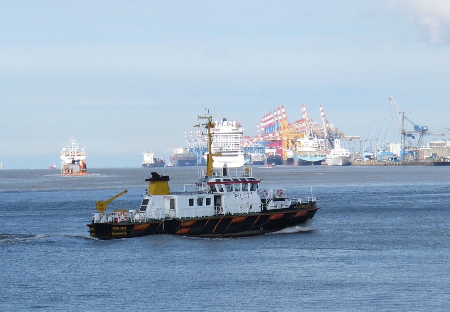 Um rebocador chamado 'KREILOTSE' em um porto, com navios de carga e guindastes ao fundo.