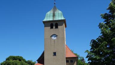 Uma igreja histórica com torre do relógio, cercada por vegetação e um caminho de pedras.