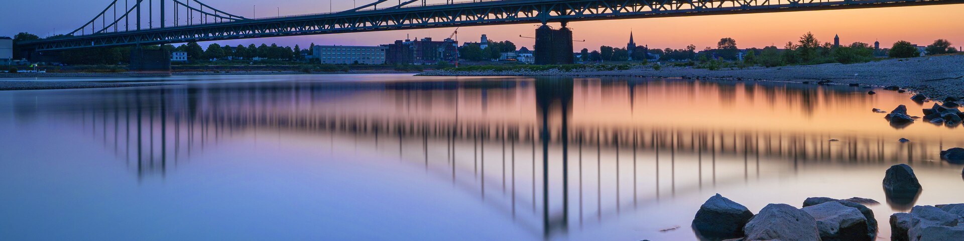 Uma ponte suspensa ao entardecer, com um rio calmo refletindo sua estrutura.