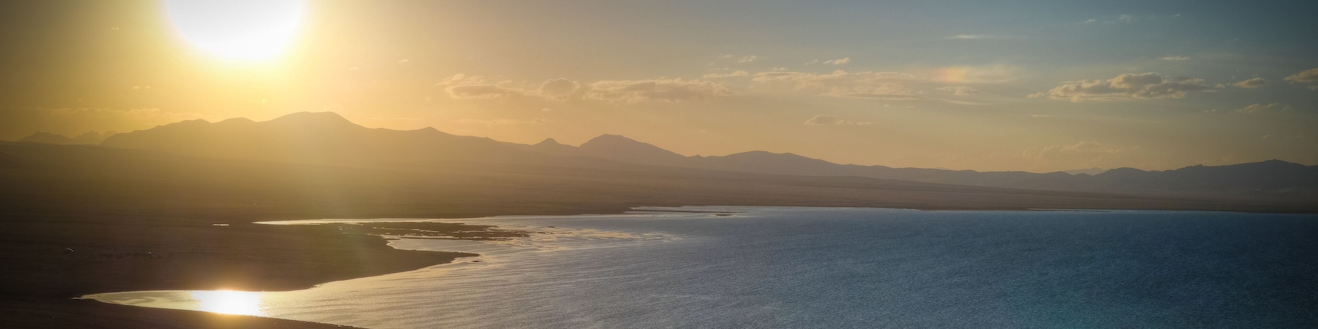 Paisagem costeira com montanhas ao fundo e um corpo d'água refletindo o sol.