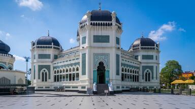 Uma grande mesquita com três cúpulas e uma entrada central.