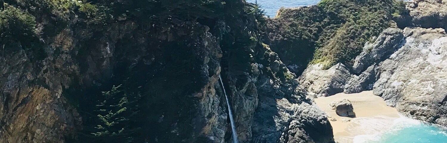 Paisagem costeira com cachoeira, praia e floresta densa.