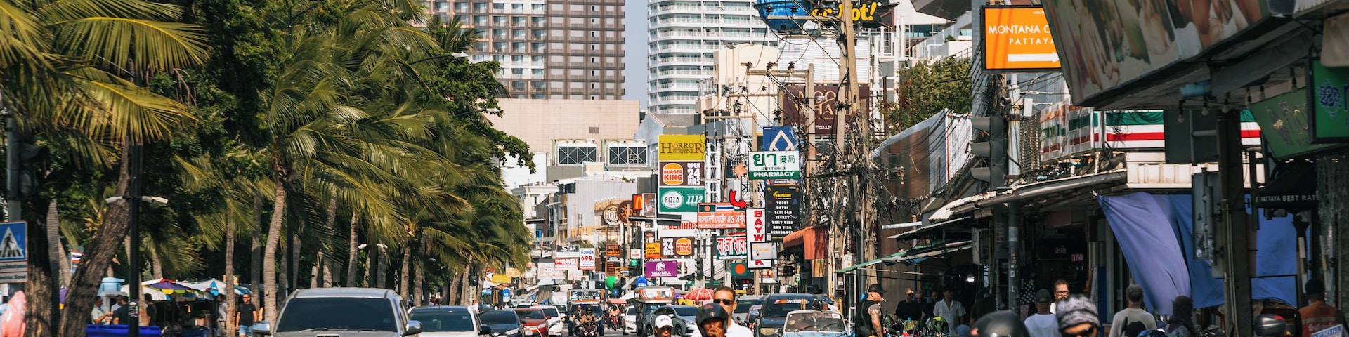 Ruas movimentadas na cidade, com palmeiras, carros, motos e diversos anúncios comerciais.