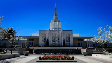 Templo Idaho Falls com uma torre, uma fonte e um jardim florido.
