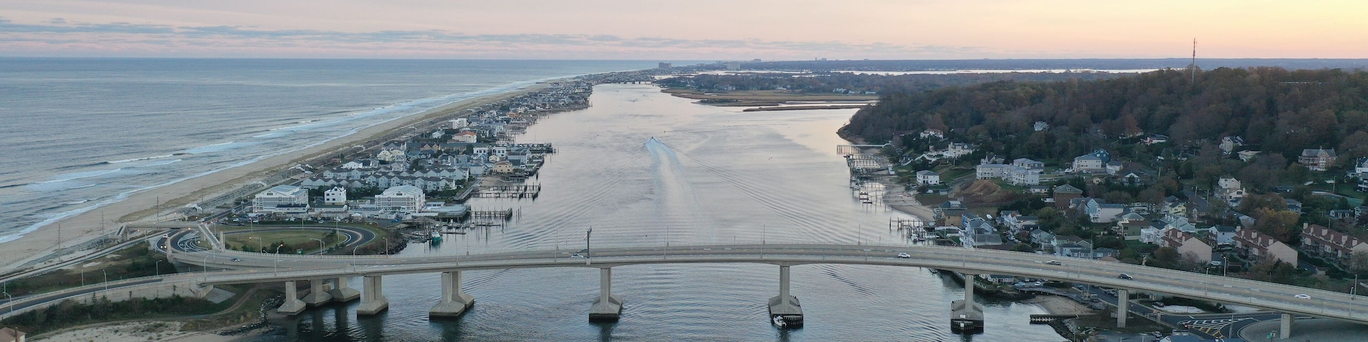Uma ponte costeira sobre um rio largo, ligando uma praia a uma cidade com edifícios e cais.