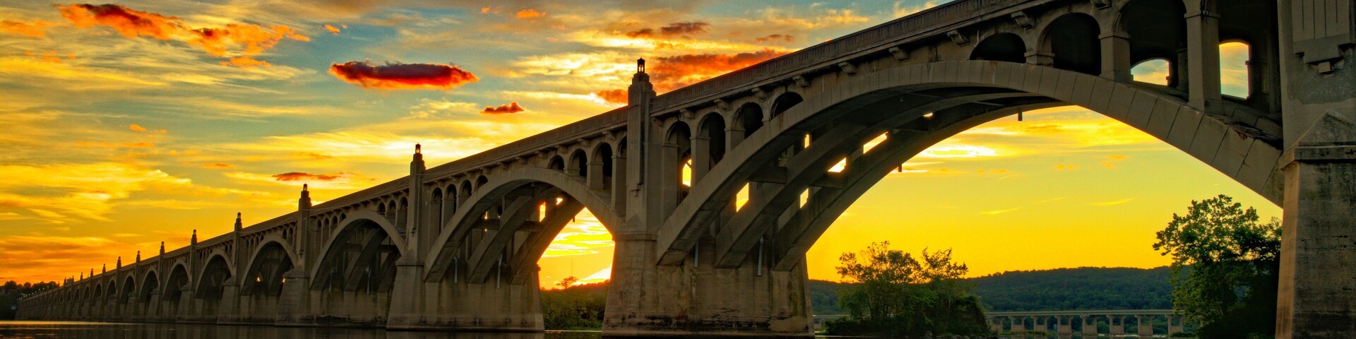 Uma ponte com várias arcos sobre um rio calmo, refletindo o céu do pôr do sol.