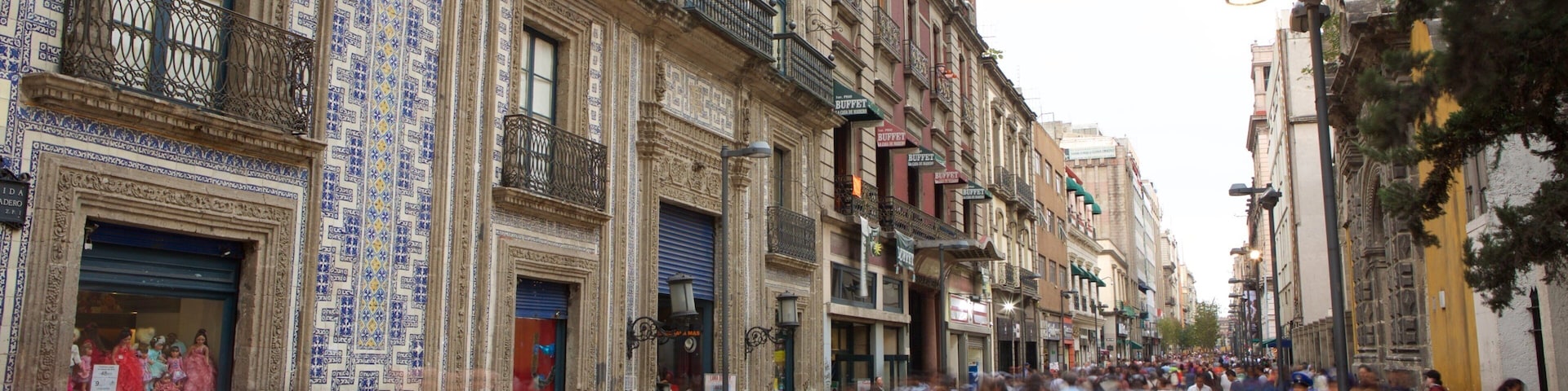 Uma rua movimentada com edifícios ornamentados, uma multidão de pessoas e uma loja de bonecas.