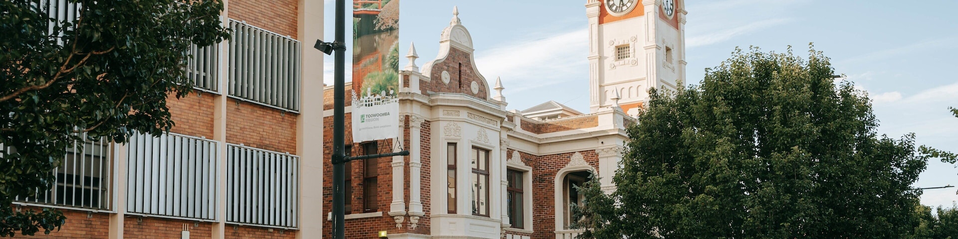 Um edifício histórico com uma torre de relógio, rodeado por árvores e edifícios modernos.