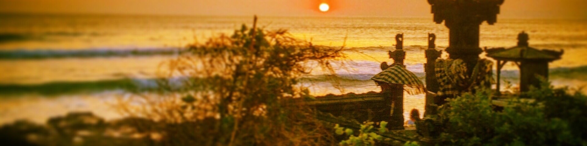 Um pôr do sol sobre o oceano, com uma estrutura tradicional em silhueta contra o céu.
