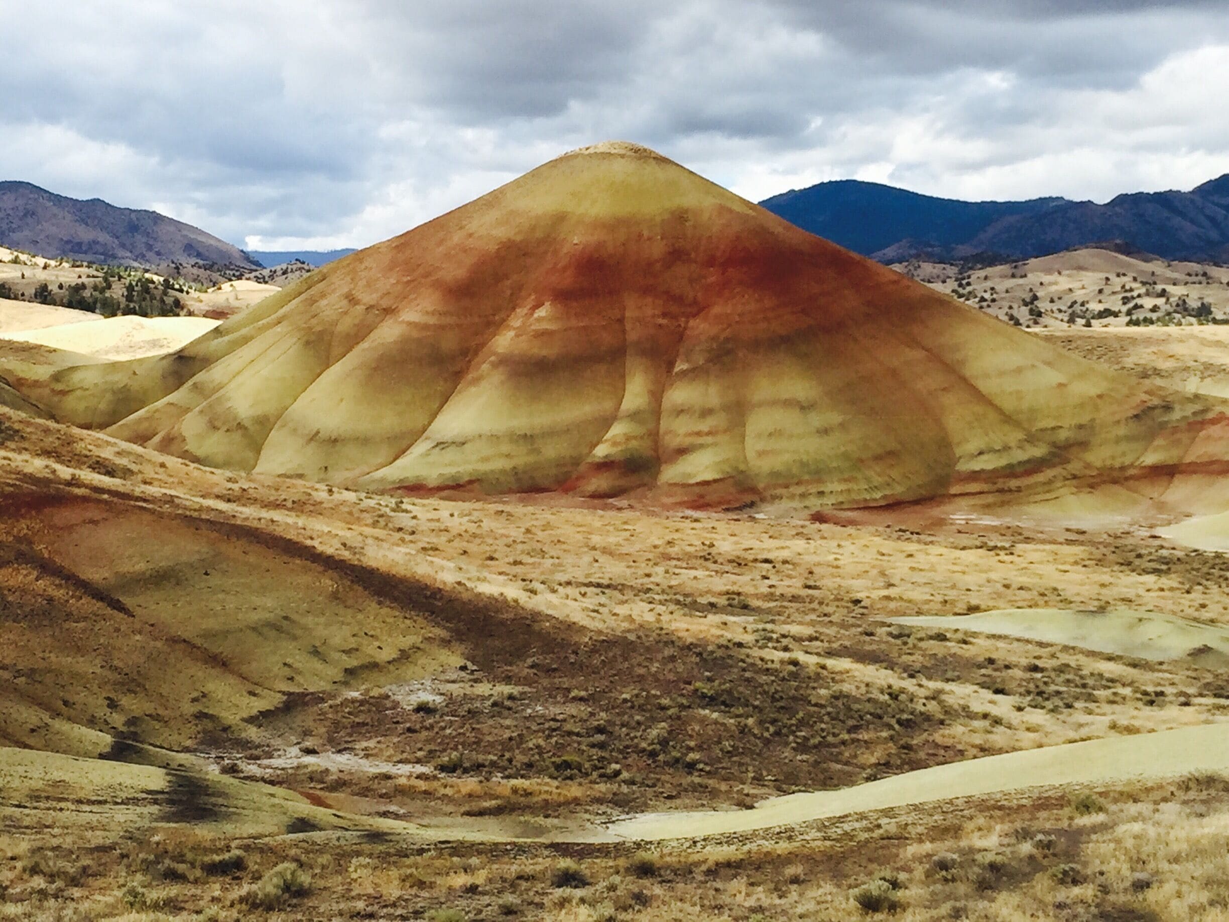 Formação geológica colorida com colinas estratificadas e montanhas ao fundo.