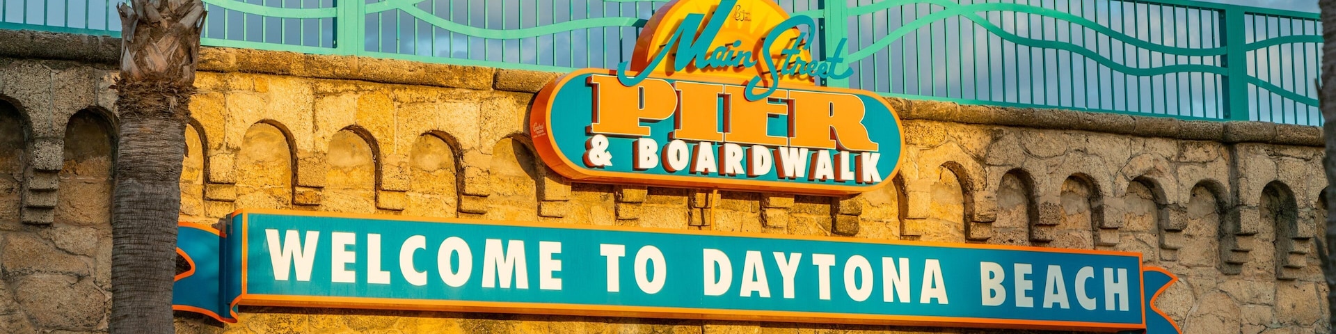 Uma ponte de pedra com uma placa que diz 'Welcome to Daytona Beach' e outra placa para 'Myrtle Street Pier & Boardwalk'.