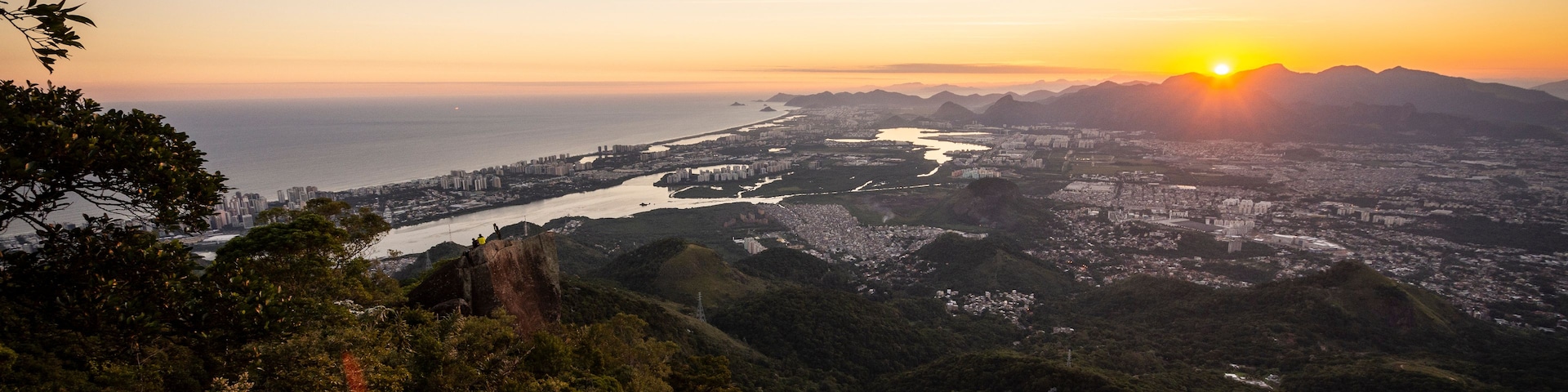 Paisagem costeira ao pôr do sol, com montanhas ao fundo.