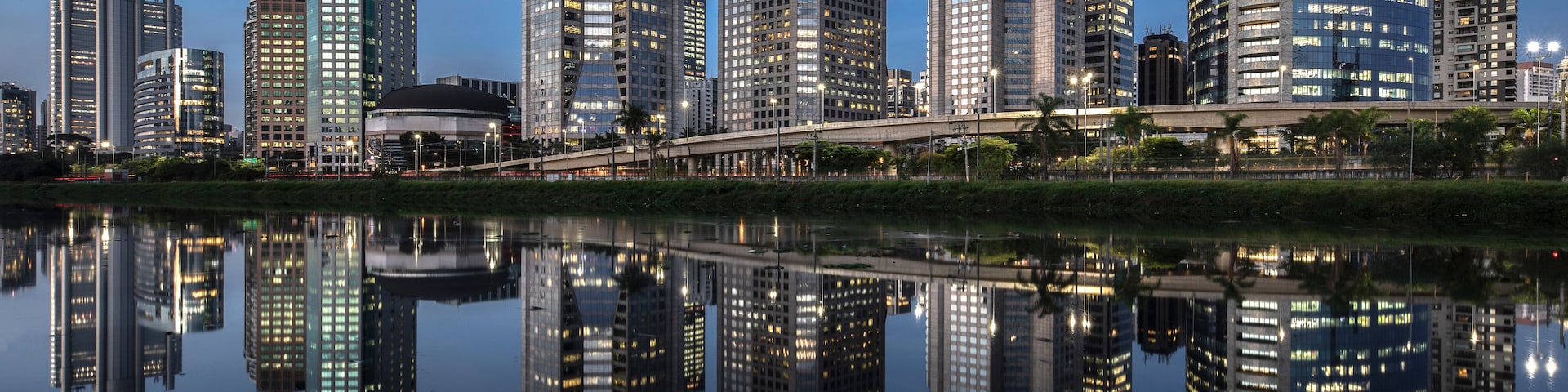 Linha do horizonte urbana com arranha-céus modernos refletidos em águas calmas.