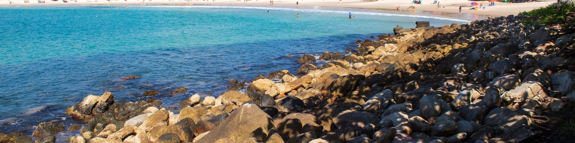 Uma linha costeira rochosa com uma praia e edifícios ao fundo.