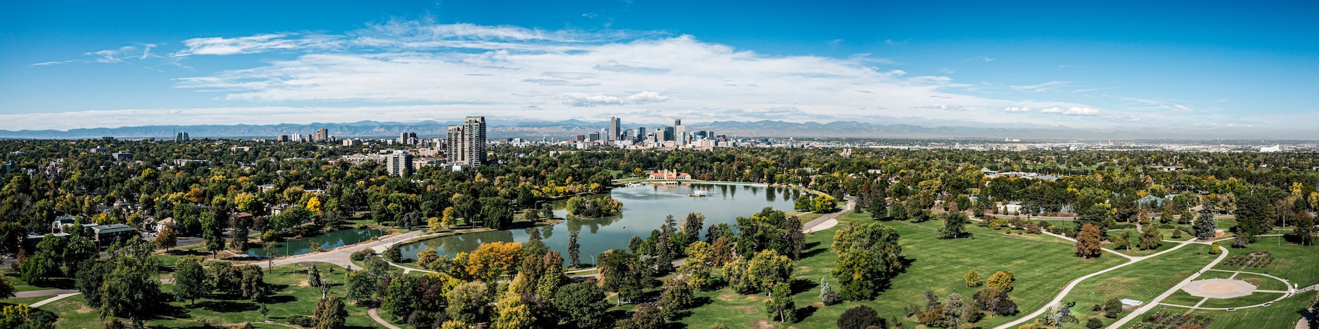 Panorama urbano com um amplo parque que inclui um lago, cercado por vegetação e edifícios da cidade.