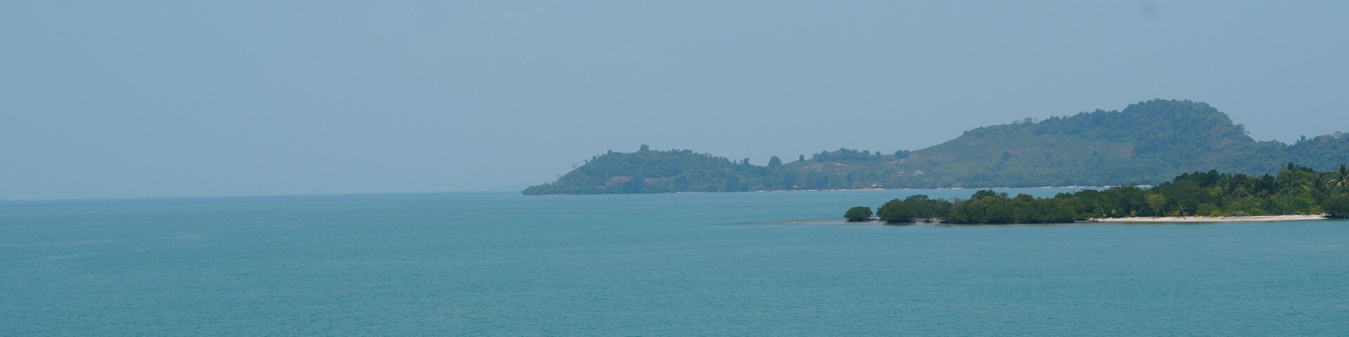 Mar calmo com uma ilha distante coberta de vegetação.