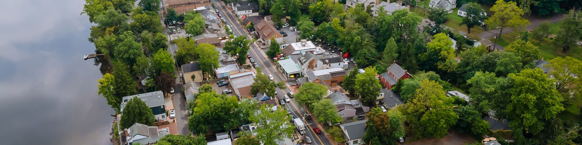 Vista aérea de uma cidade às margens do rio, com muita vegetação, uma avenida principal e vários edifícios.