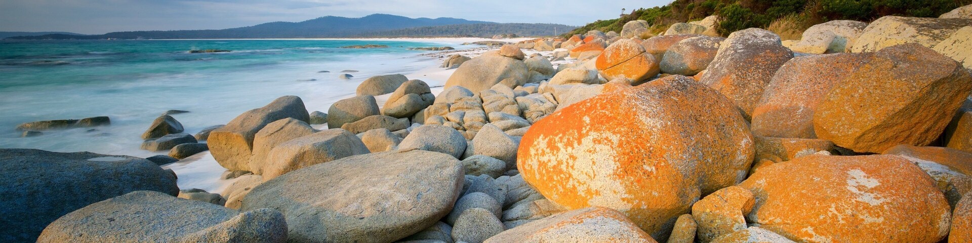 Uma praia rochosa com grandes pedregulhos e vista clara do oceano.