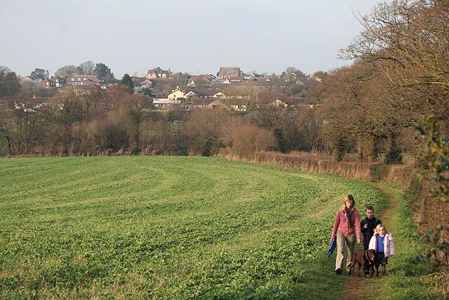 Uma família caminhando em um campo verde, com casas ao fundo.