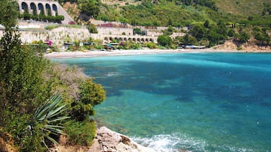 Uma vila costeira com águas azul-claras, uma praia arenosa e um edifício histórico com arcos.